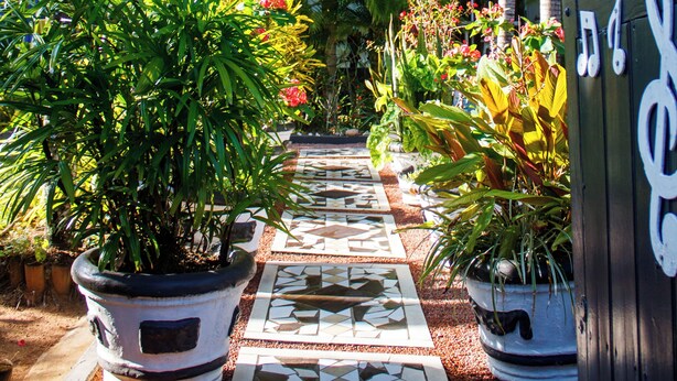 Caminho ladeado por plantas em vasos e um pavimento de azulejos.