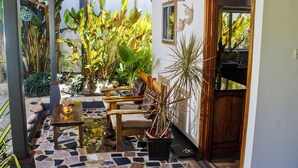 Alpendre coberto com um banco de madeira, uma mesa pequena e plantas em vasos.