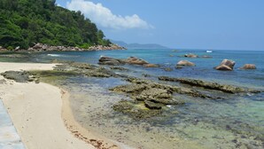 Uma praia com águas claras, pedras e uma colina arborizada.