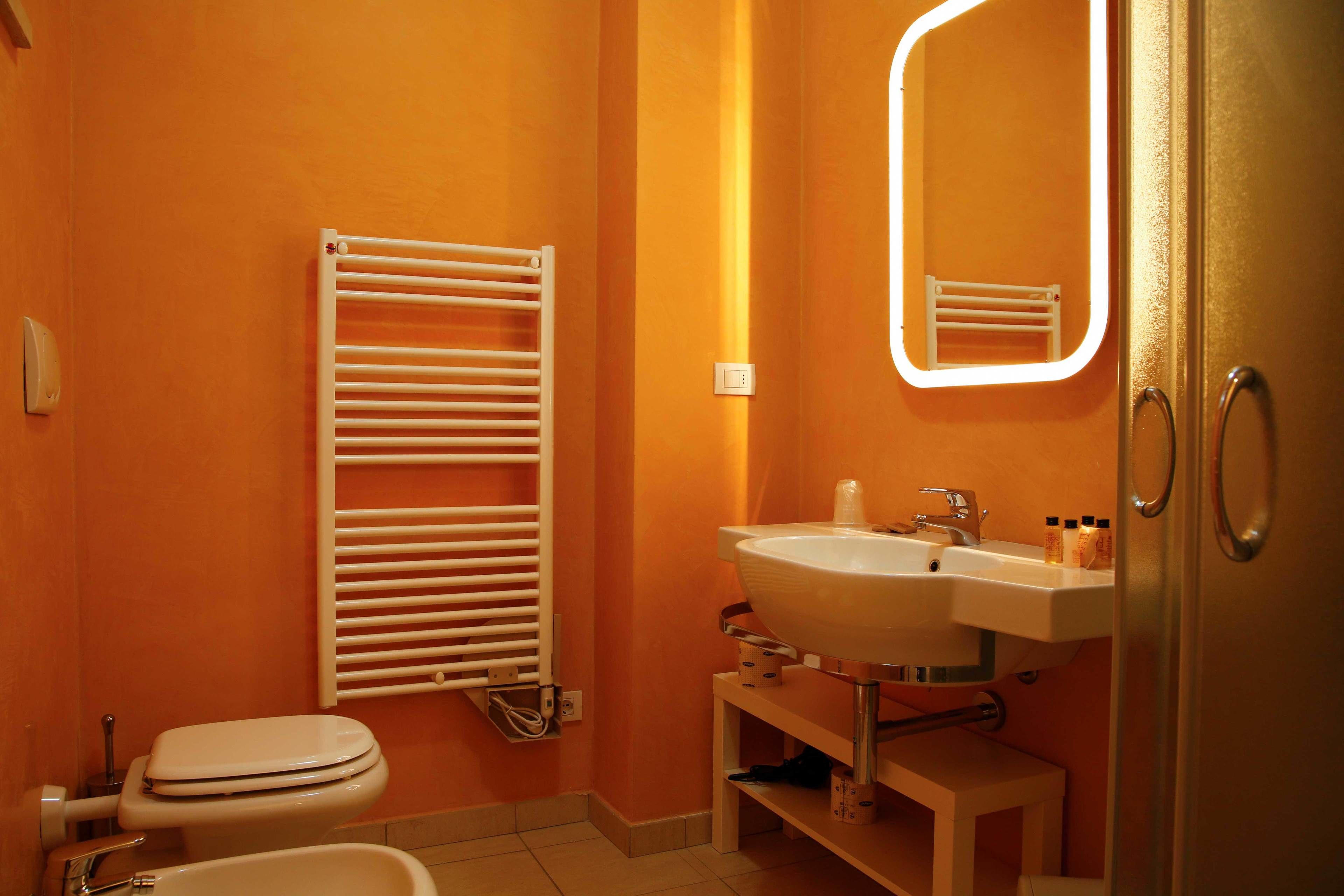 Casa de banho com sanita branca, lavatório com espelho e um porta-toalhas.