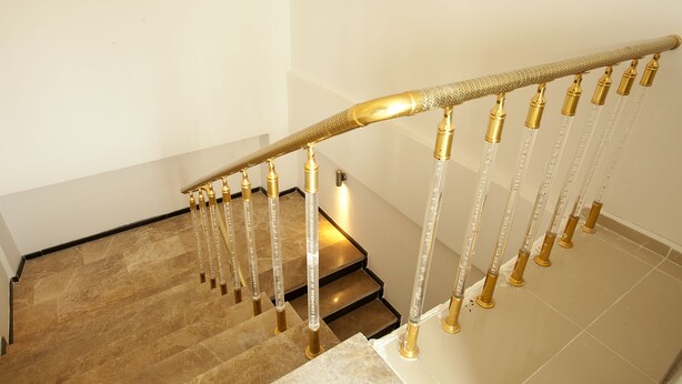 Escada com corrimão dourado e balaústres de vidro transparente.