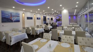 Restaurante com várias mesas preparadas para refeições, com interior moderno, iluminação embutida e obras de arte nas paredes.