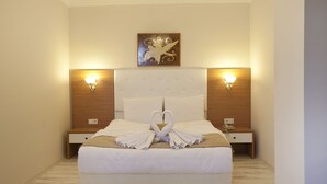 Uma cama bem arrumada com arranjo de toalhas em formato de coração, uma cabeceira de madeira e duas luminárias laterais.