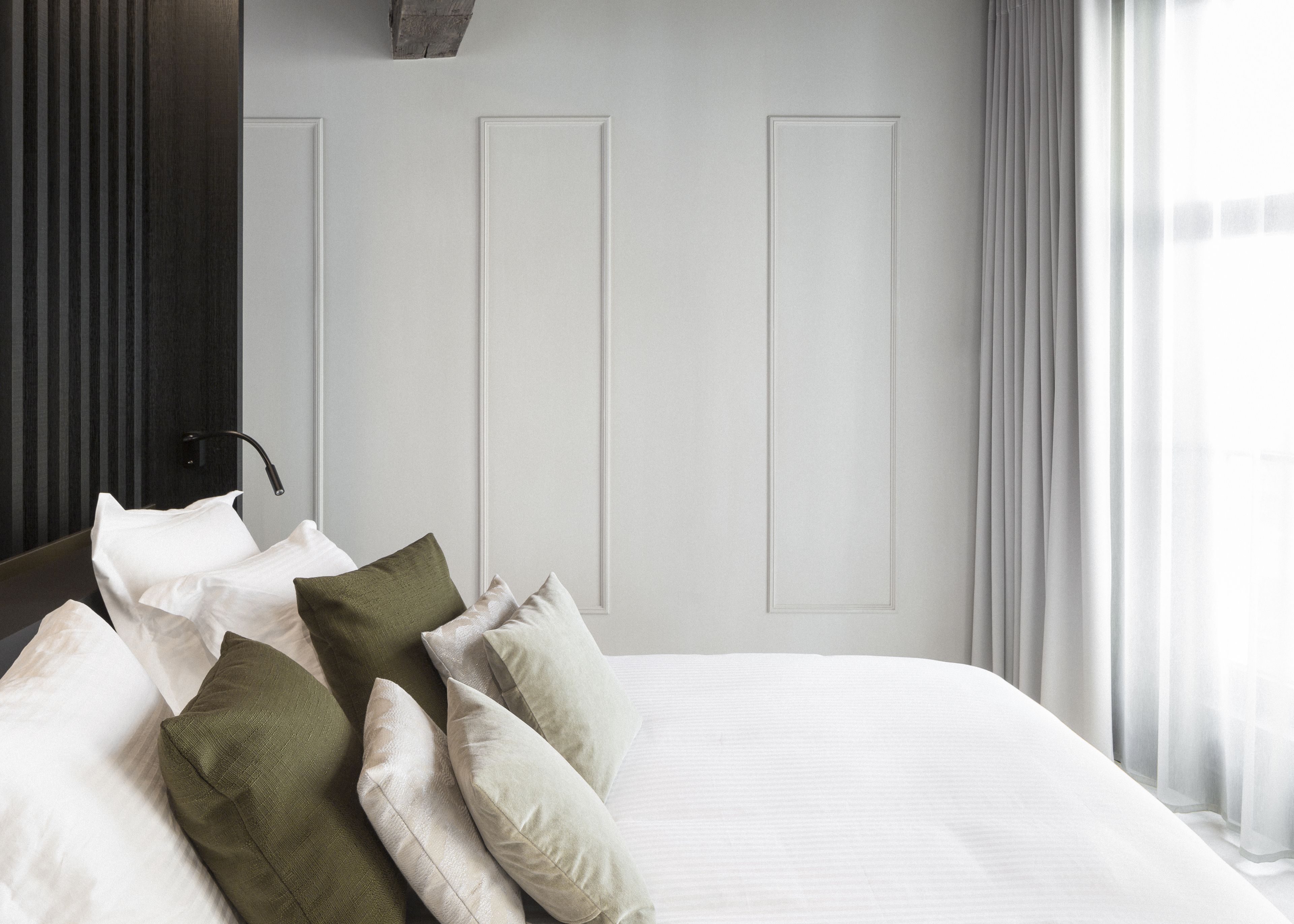 Quarto de hotel com uma cama grande, roupa de cama branca e várias almofadas.