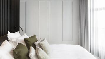 Quarto de hotel com uma cama grande, roupa de cama branca e várias almofadas.