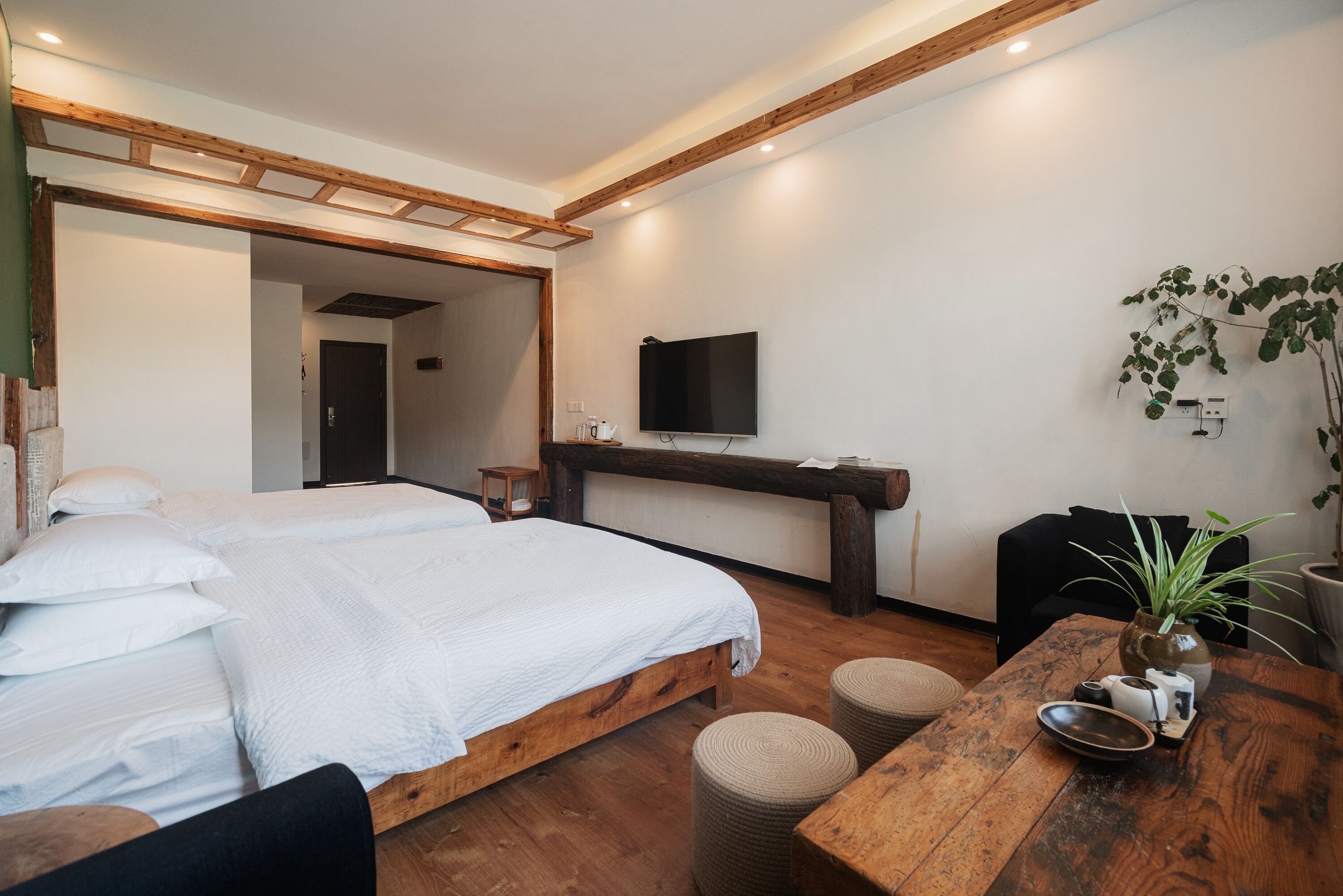 Quarto com uma cama grande, uma escrivaninha de madeira, televisão e uma planta.