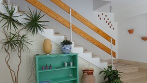 Uma escada com corrimãos de madeira, uma prateleira verde com diversos objetos e plantas em vasos.