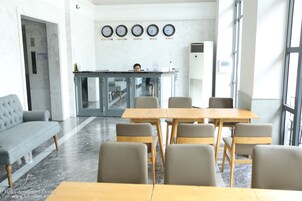 Um saguão de hotel com balcão de recepção, um sofá e uma área de refeições com cadeiras e uma mesa.