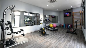 Uma academia com equipamentos de ginástica, esteira e televisão na parede.