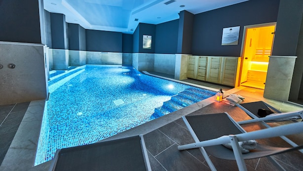 Piscina interna com chão em mosaico azul, cercada por paredes e teto com iluminação embutida.