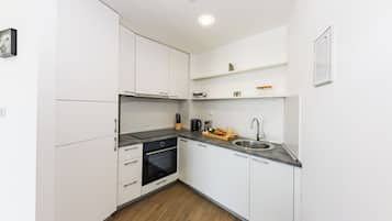 Uma cozinha compacta com armários brancos, forno embutido, pia de aço inoxidável e bancada com diversos utensílios de cozinha.