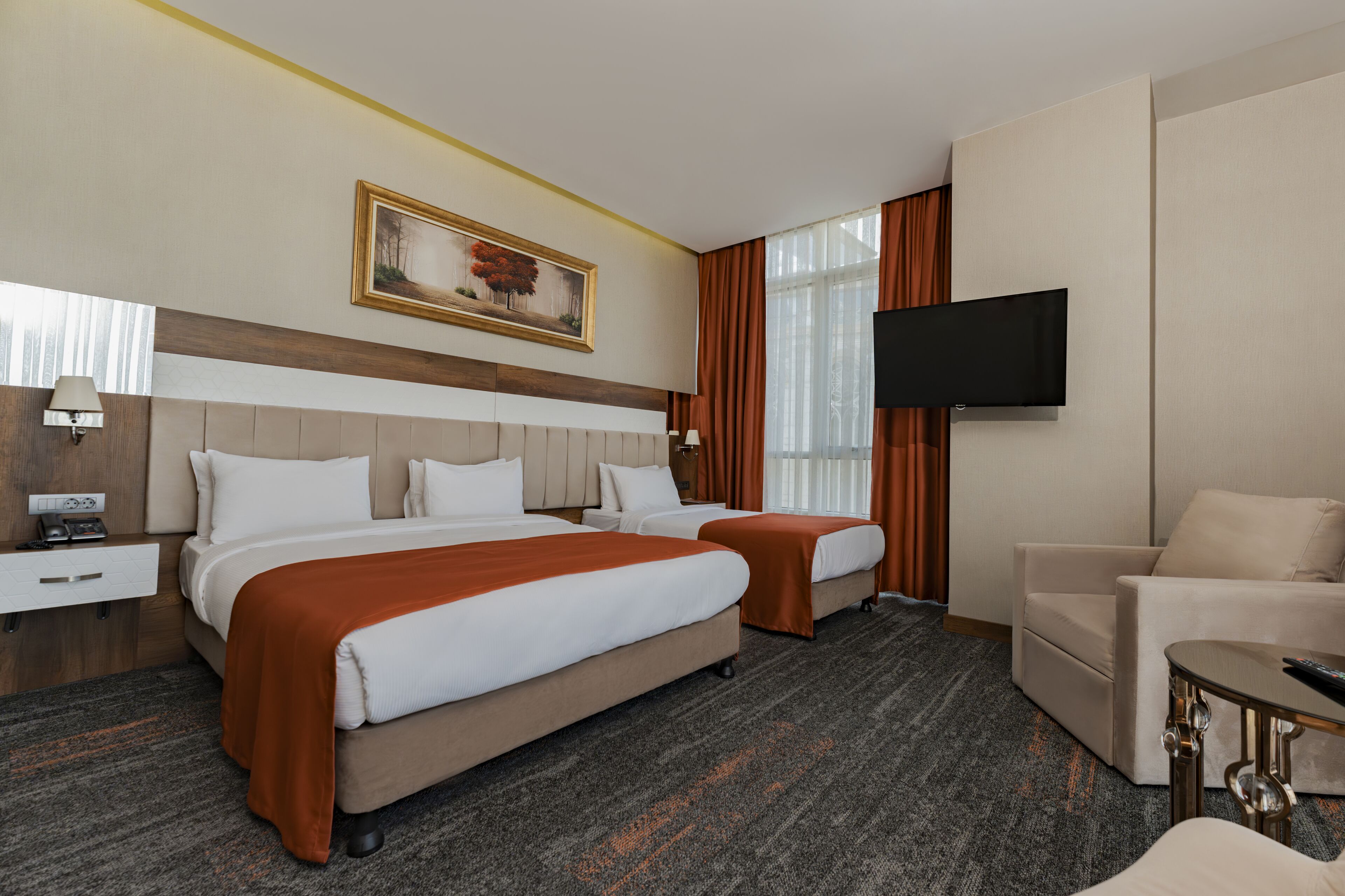 Quarto de hotel com duas camas, um sofá, uma TV e um quadro na parede.