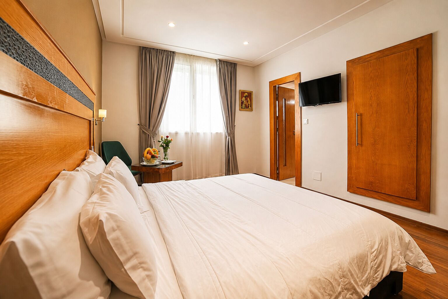 Quarto de hotel com uma cama grande, uma mesa de trabalho com abajur, televisão e guarda-roupa.