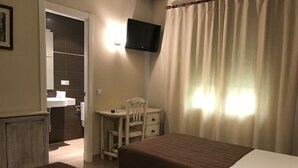 Quarto de hotel com duas camas, uma escrivaninha, uma cadeira, uma televisão e um banheiro visível por uma porta aberta.