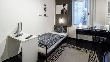 Um quarto com cama, escrivaninha, cadeira, radiador e janela com cortinas.