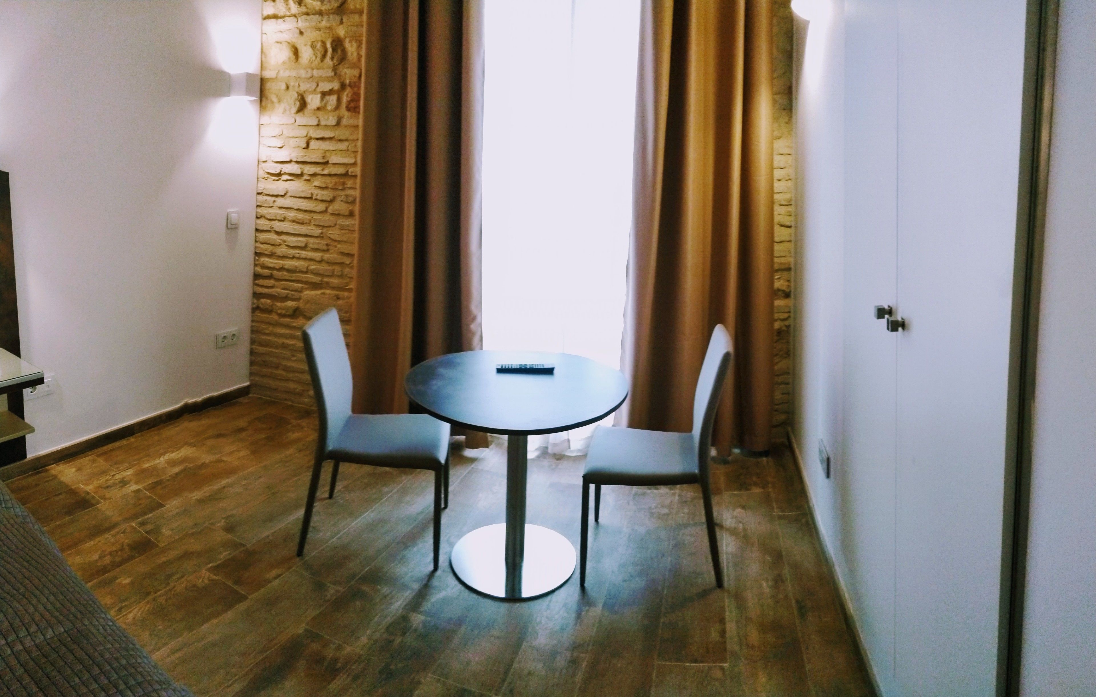 Um quarto pequeno com uma mesa redonda e duas cadeiras, uma parede de pedra e uma porta.