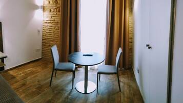 Um quarto pequeno com uma mesa redonda e duas cadeiras, uma parede de pedra e uma porta.