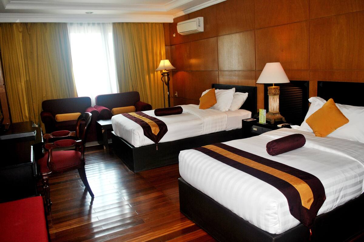 Quarto de hotel com duas camas, uma escrivaninha, uma cadeira e um abajur.