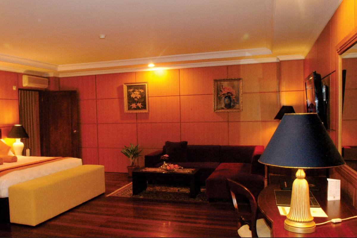 Quarto de hotel com cama, sofá, mesa de centro e escrivaninha com luminária.