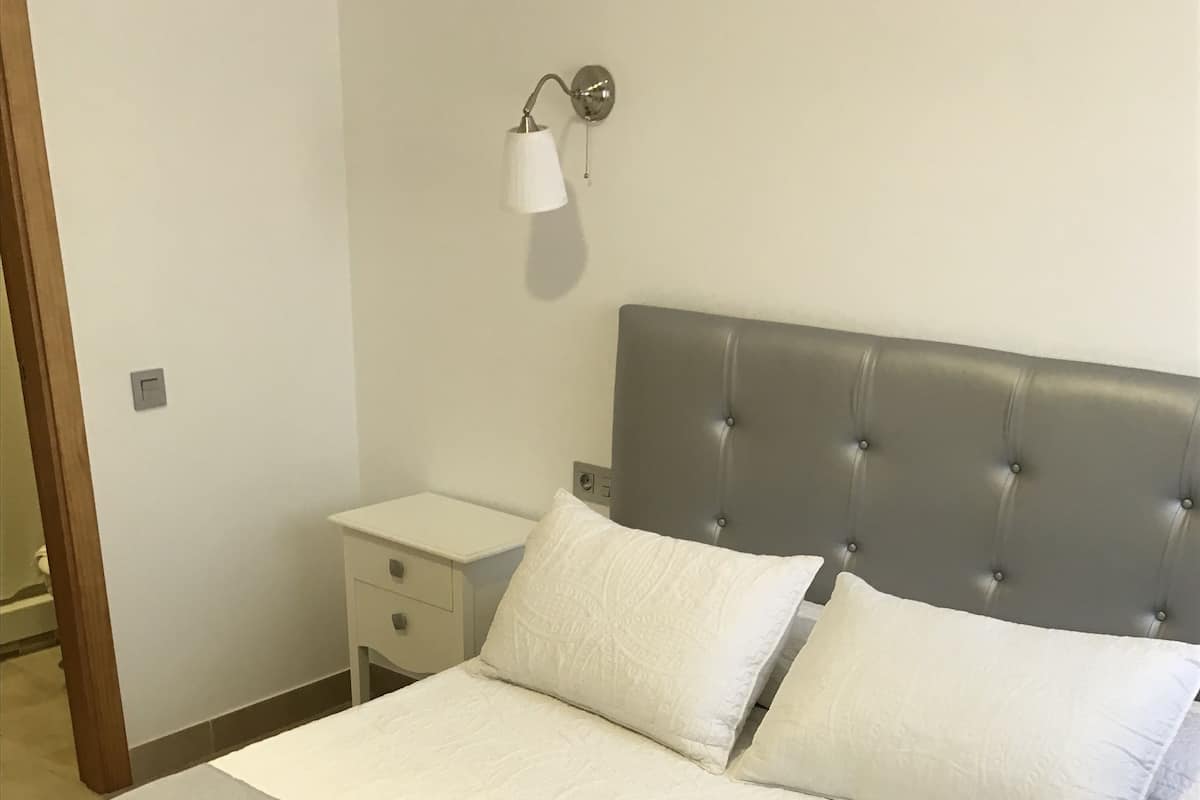Cama bem arrumada com cabeceira cinza, almofadas brancas e roupão branco sobre a cama.