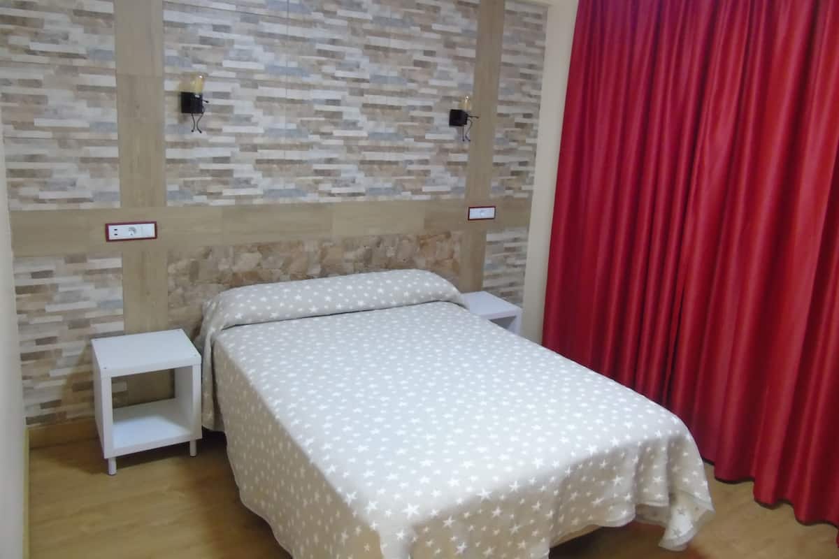 Quarto com cama, mesas de cabeceira, cortina vermelha e parede com desenho estampado.