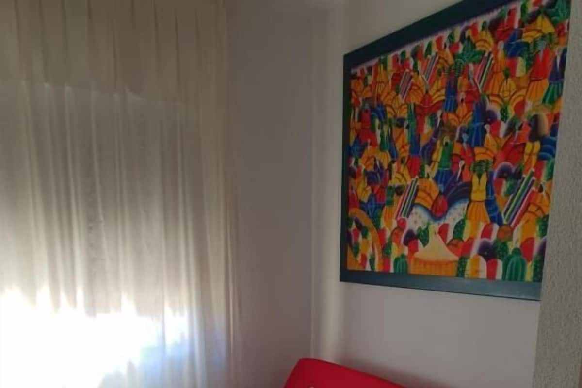 Quarto com sofá vermelho, mesa de centro de vidro e uma pintura abstrata colorida na parede.