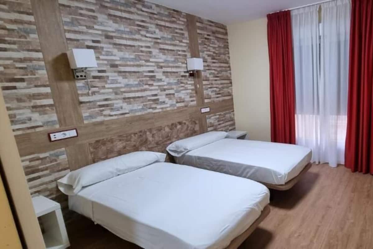Quarto de hotel com duas camas, cabeceira de madeira, televisão e cortina vermelha.