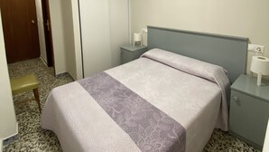 Quarto bem organizado com cama, mesas de cabeceira, uma cadeira e uma porta.