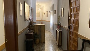 Um corredor com porta de madeira, balcão de recepção, quadros nas paredes e uma cama com um cobertor dobrado.