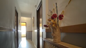 Um corredor com piso de azulejos, um banco de madeira e um vaso com flores sobre um aparador.