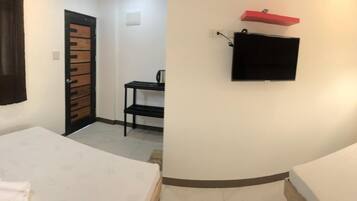 Quarto de hotel com uma cama, uma escrivaninha, uma cadeira, uma televisão na parede e uma porta com um aviso.