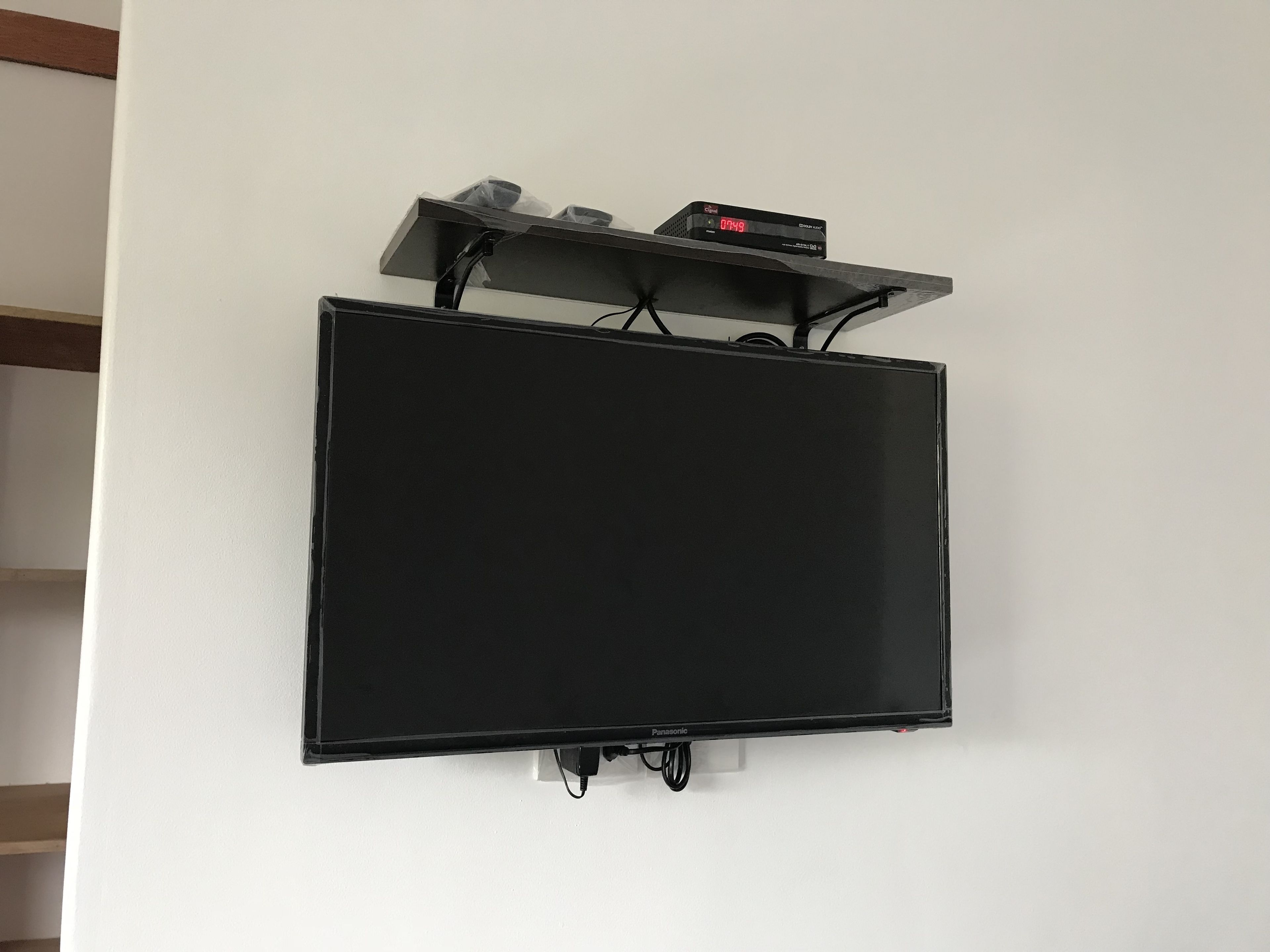 Uma televisão de tela plana presa na parede, com um relógio digital acima, ligada a um filtro de linha.
