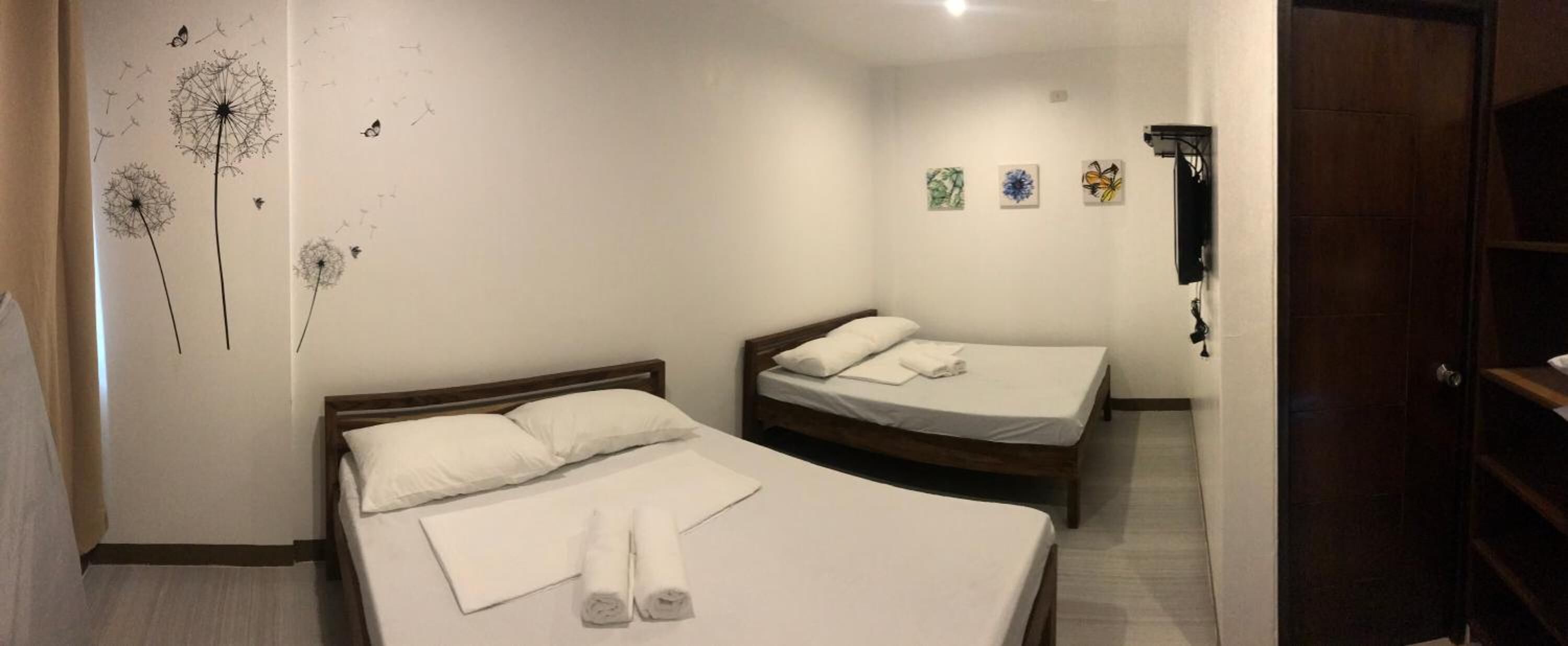 Quarto de hotel com duas camas, um painel de cabeceira de madeira, uma televisão fixada na parede e obras de arte.