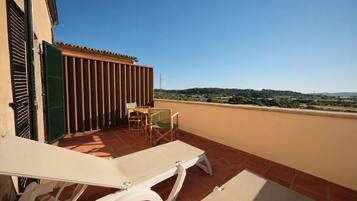 Uma varanda com mesa e cadeiras, vista para o campo e um edifício com telhado de telhas.