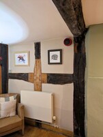 Quarto com vigas de madeira aparentes, um radiador, um sofá de couro marrom e duas molduras na parede.
