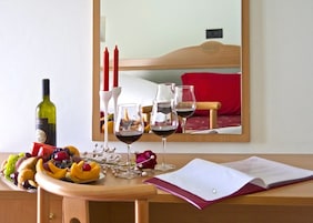 Uma mesa bem arrumada com uma garrafa de vinho, copos, uma tábua de frutas e um livro.