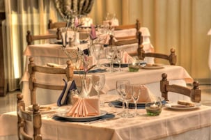 Mesa de jantar formal posta com cadeiras, copos e um arranjo central.