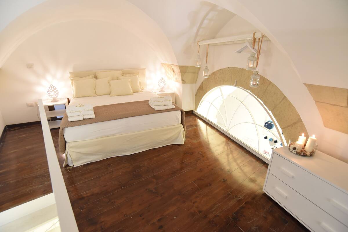 Quarto com cama, mesas de cabeceira e cómoda branca.