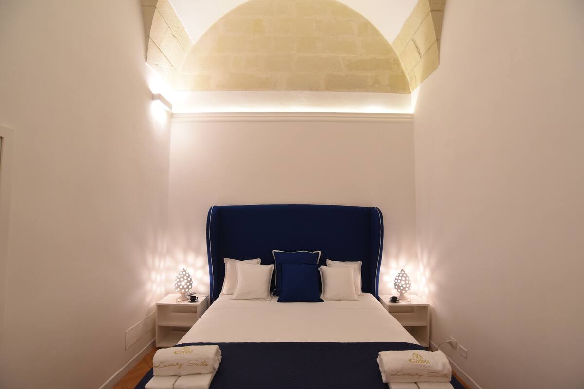 Quarto de hotel com uma cama grande, duas mesas de cabeceira e um arco de pedra acima da cama.