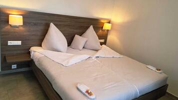 Cama bem arrumada com almofadas, mesa de cabeceira e duas luminárias fixadas na parede.