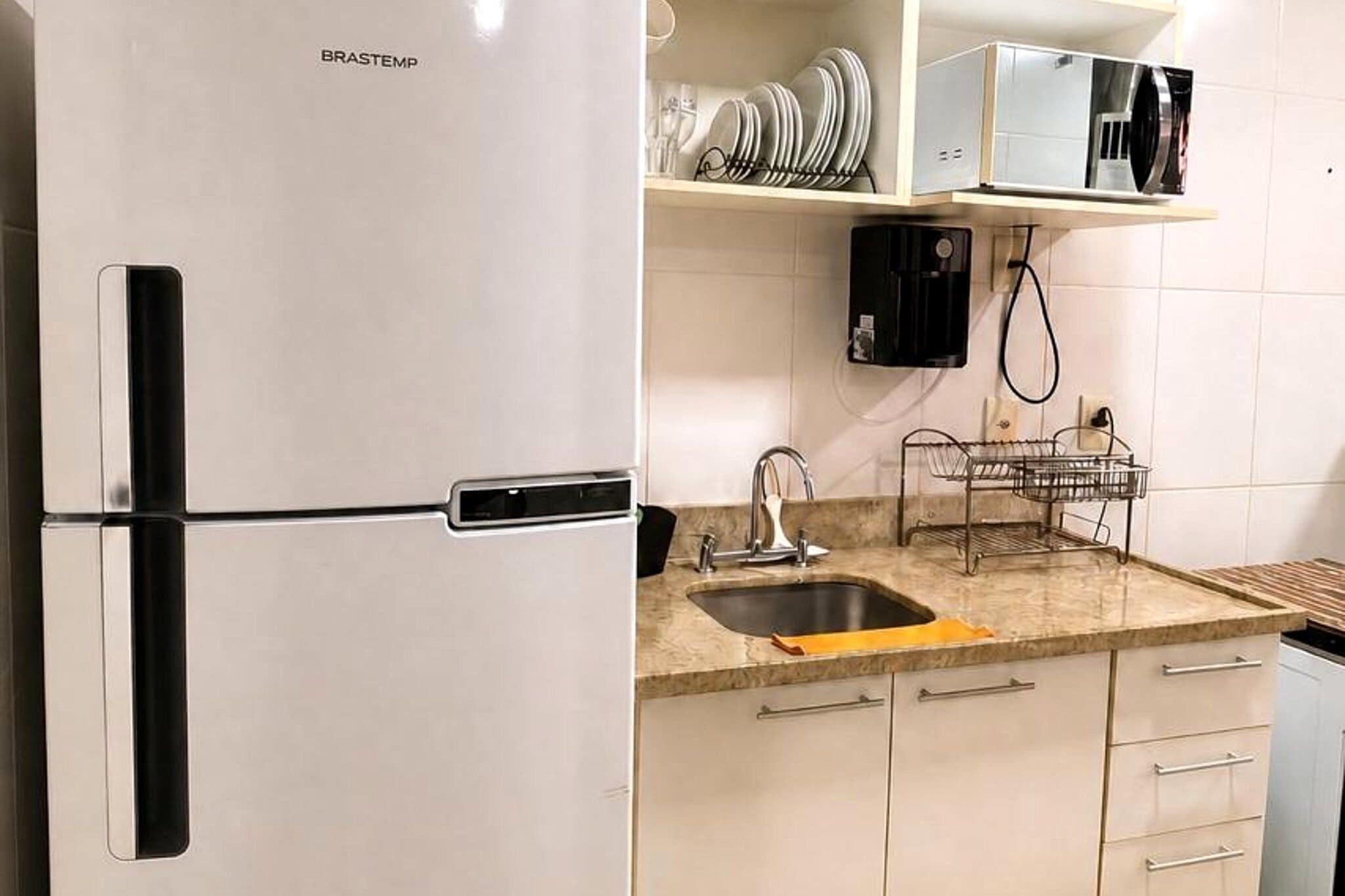 Cozinha com geladeira branca, pia e micro-ondas na bancada.