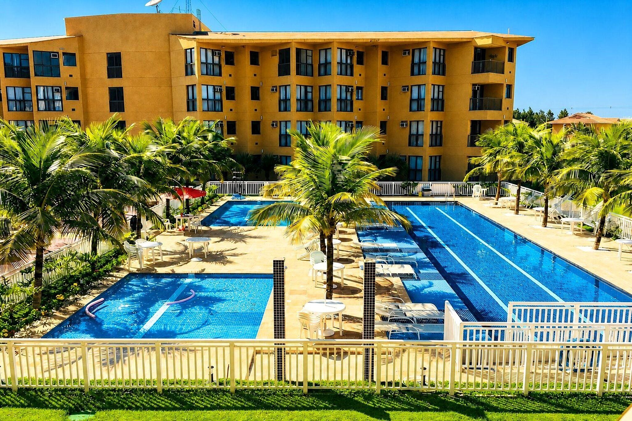 Hotel com várias piscinas, palmeiras e um céu azul cristalino.