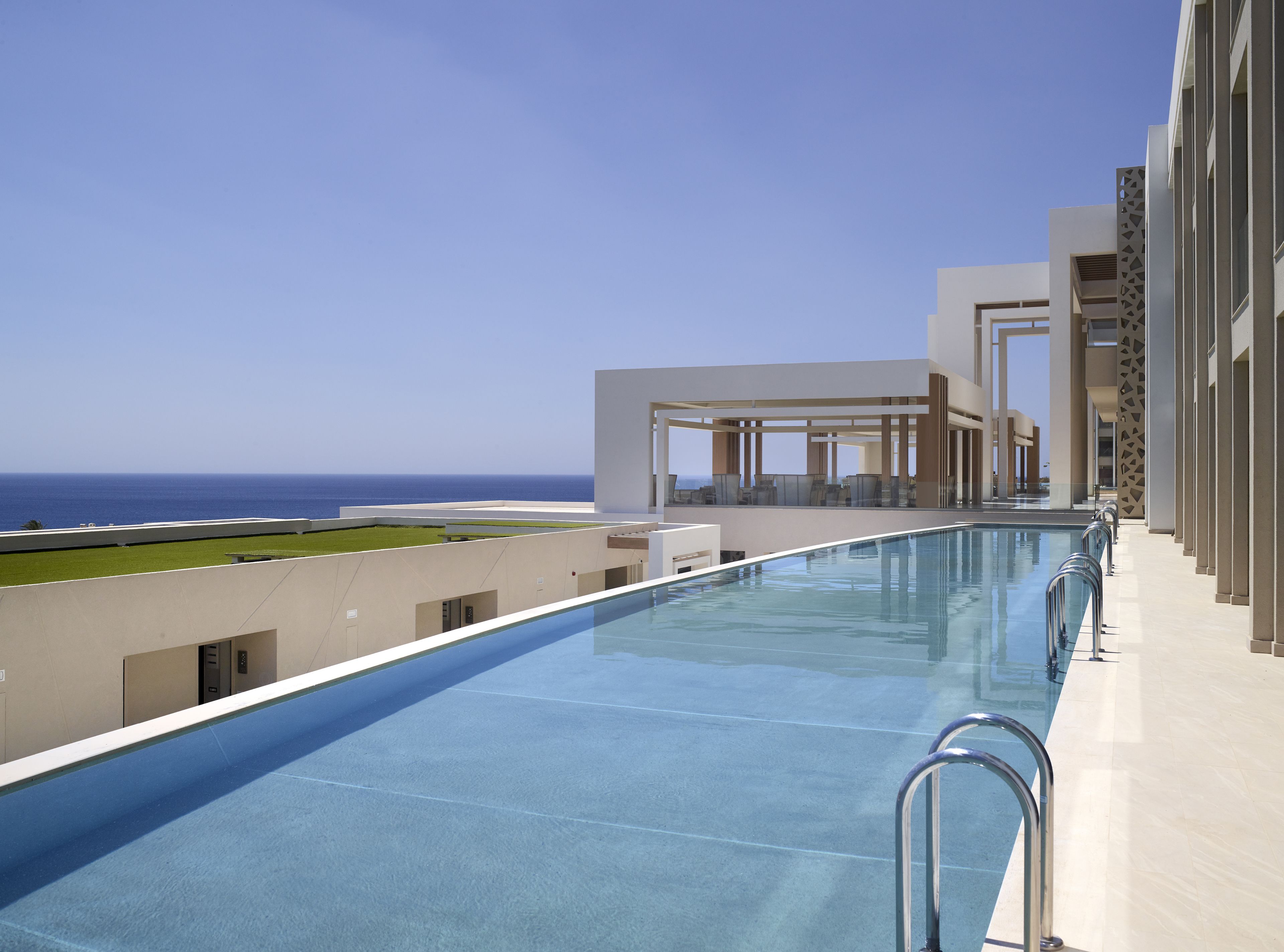 Piscina infinita moderna com vista clara do oceano, área de estar coberta e design arquitetônico minimalista.