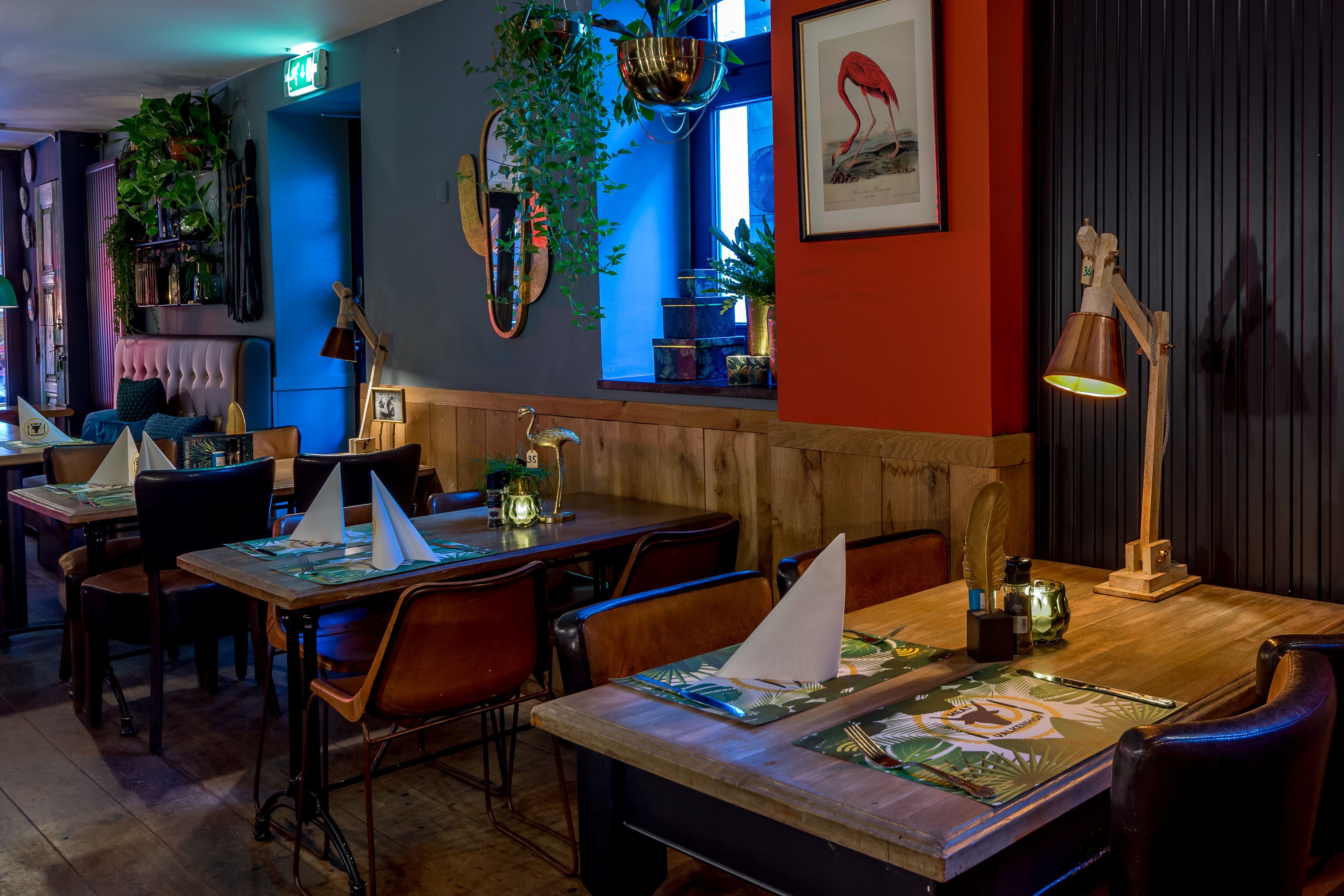 Um restaurante com mesas e cadeiras de madeira, além de plantas e decorações diversas nas paredes.