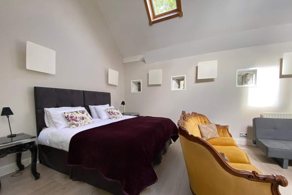 Quarto com cama, mesa de cabeceira, cadeira, sofá e janela.