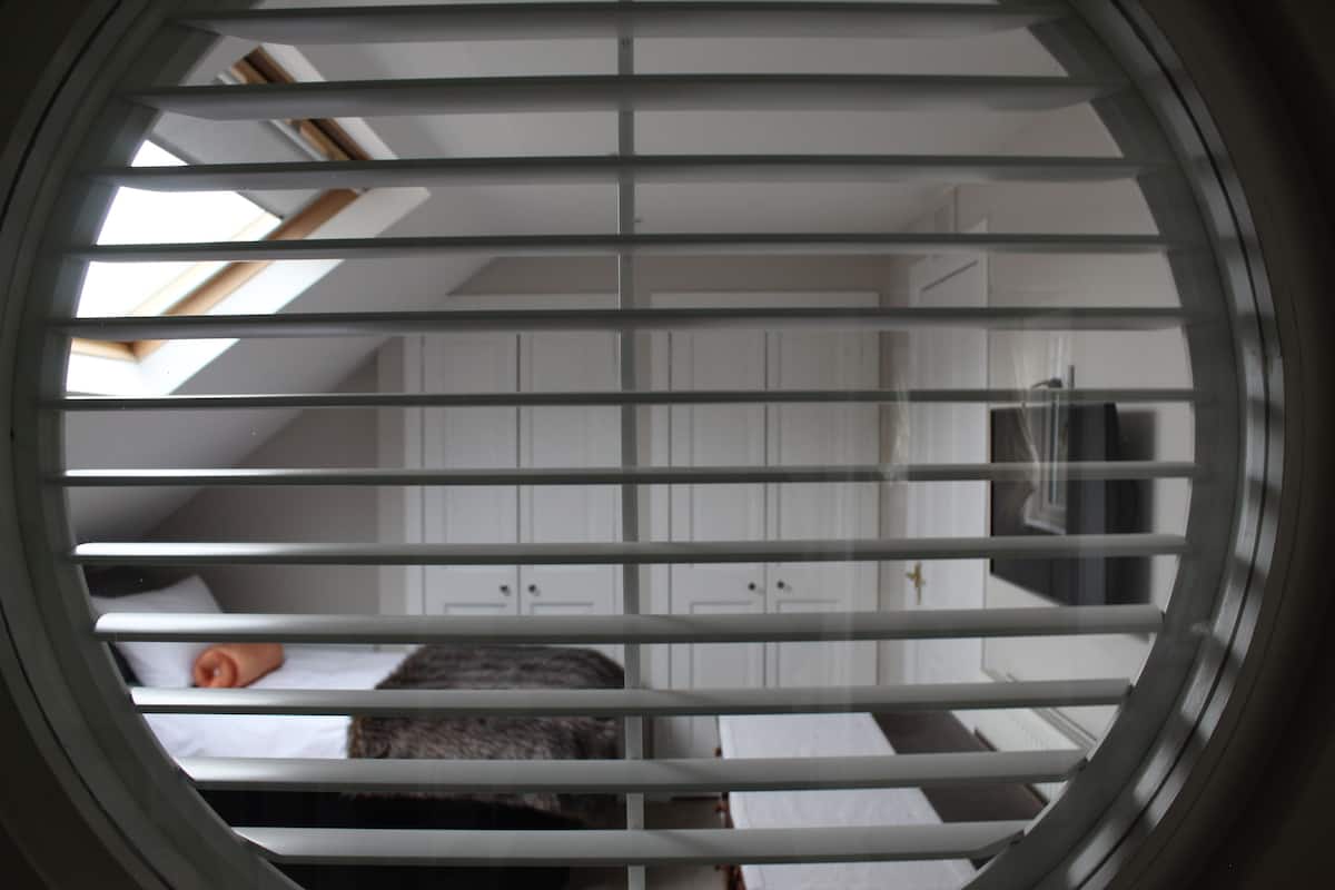 Quarto com claraboia, paredes brancas e cama com cabeceira cinza.
