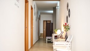 Um corredor com porta de madeira, uma mesa pequena com um vaso de flores e uma cadeira.