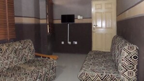 Quarto com dois sofás estampados, porta de madeira, televisão na parede e um relógio.