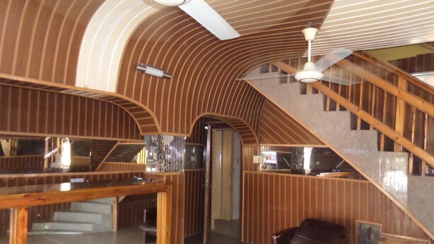 Um interior espaçoso com teto de madeira curvada, uma escadaria e um balcão de recepção.