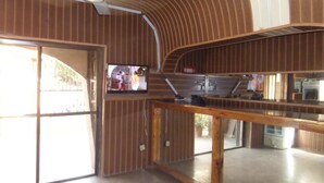 Um quarto espaçoso com teto de madeira curvo, ventilador de teto, televisão na parede e uma grande janela que oferece luz natural.